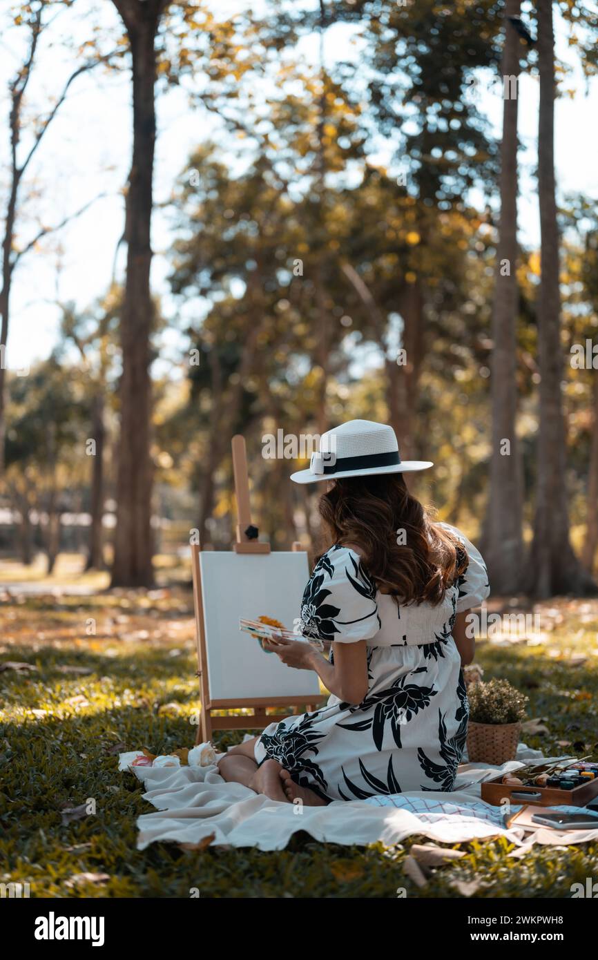 Calm young woman in casual clothes painting picture in autumn park ...