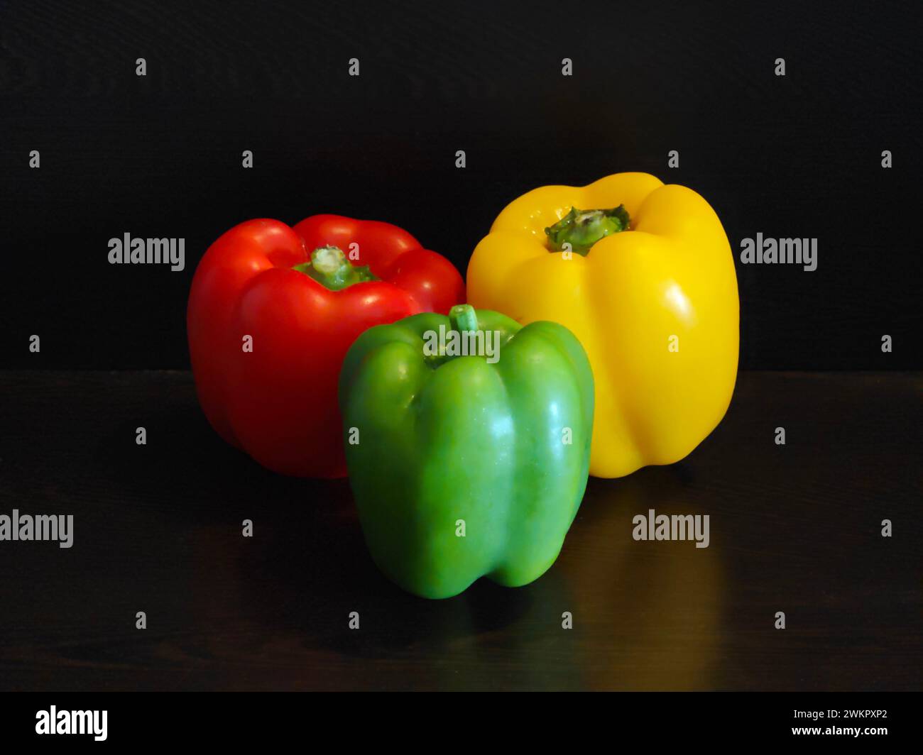 Three peppers arranged in a row on a sleek black tabletop Stock Photo ...