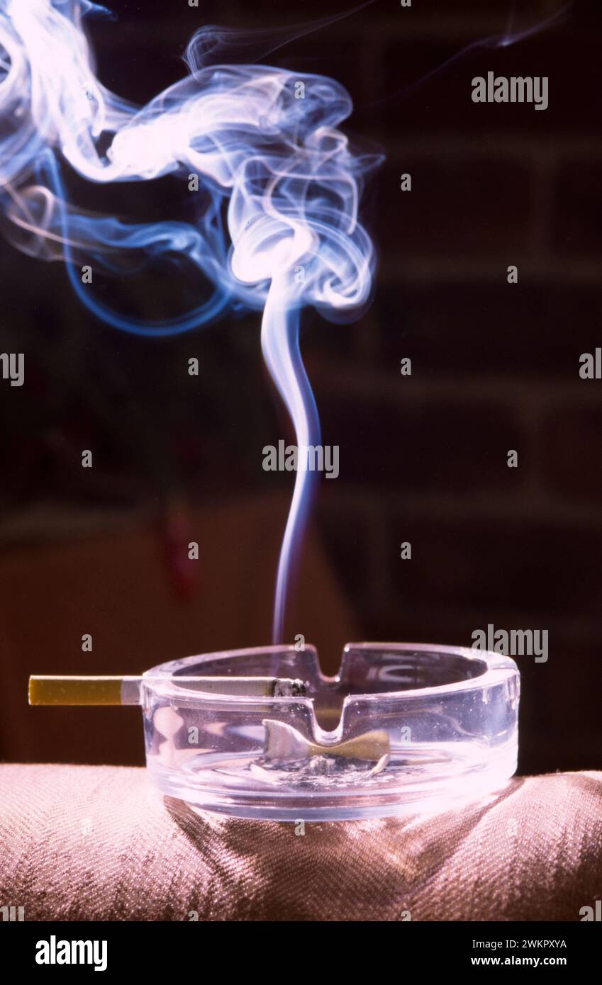 smoke from a cigarette curling up into the air from an ashtray, indoor ...