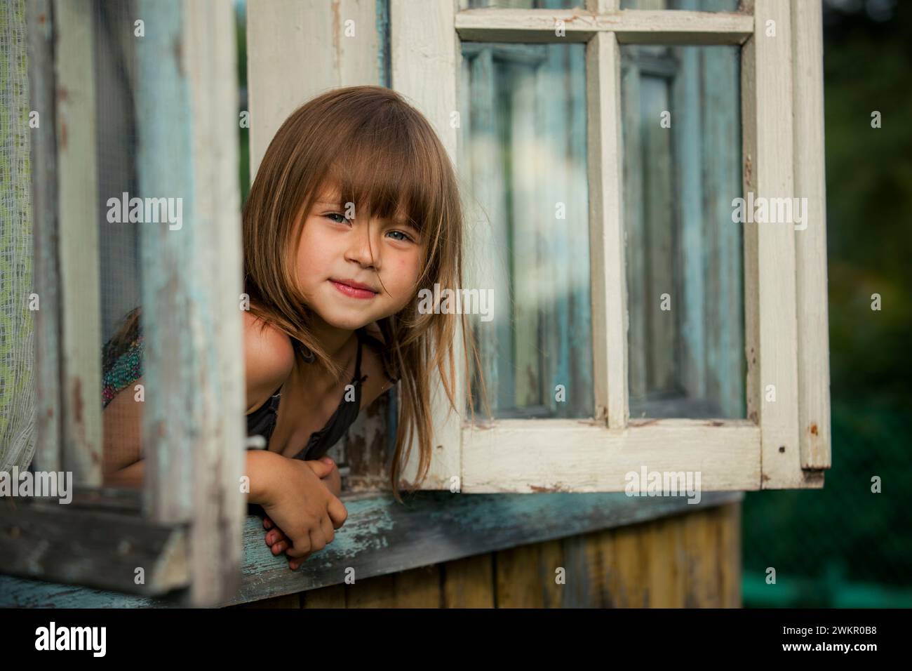 Portrait of a sweet little girl looking out the window of a house in ...