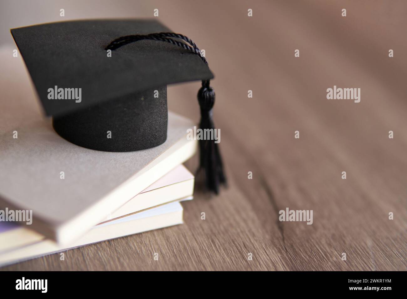 Graduation cap on top of stack of books on a wooden table. Copy space ...