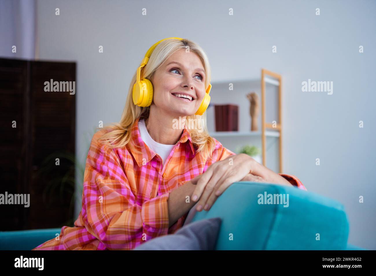 Photo of positive cheerful olf lady sit couch listen wireless headset ...
