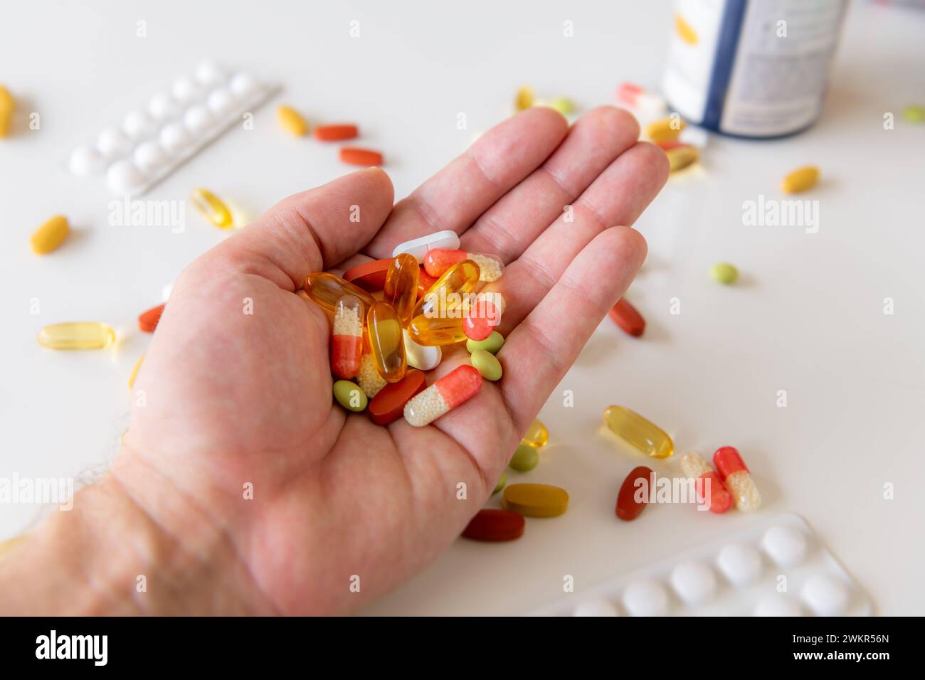 A male human hand holding pile of colourful medicine pills with white ...