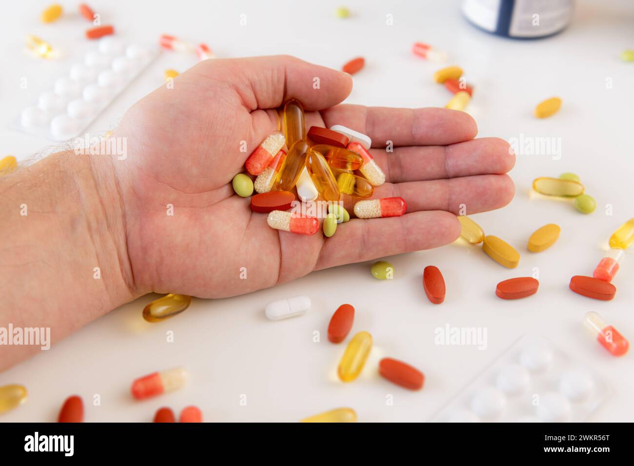 A male human hand holding pile of colourful medicine pills with white ...