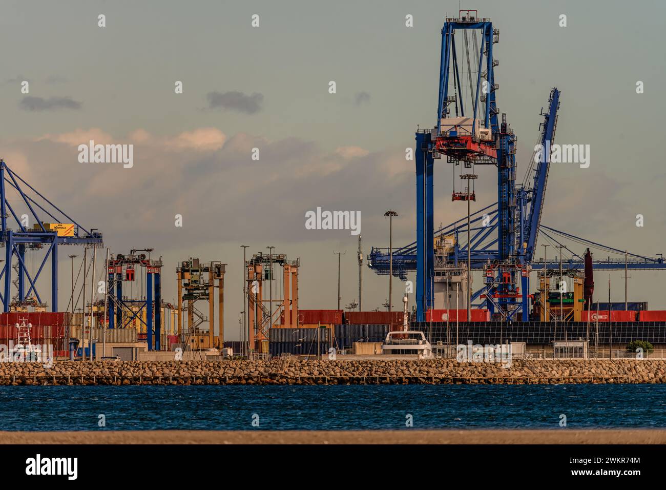A bustling industrial port shows the activity of trade with container cranes ready to load and ...