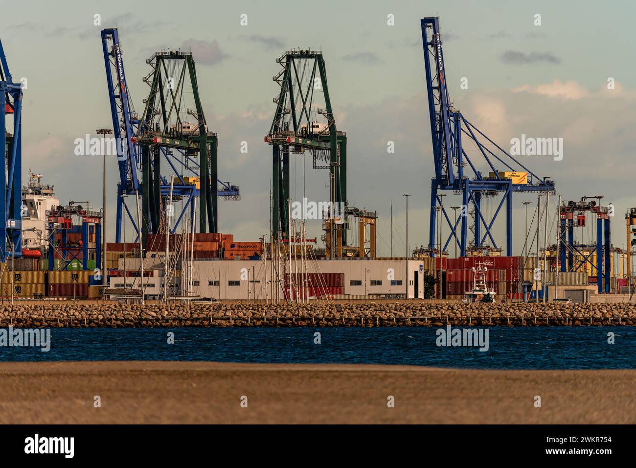 A bustling industrial port shows the activity of trade with container cranes ready to load and ...