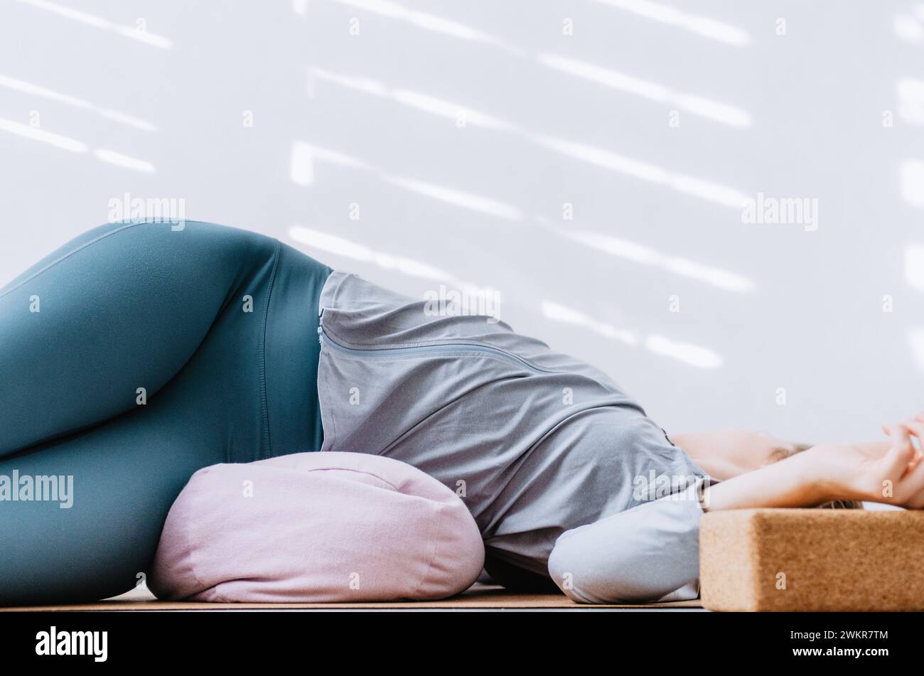 Woman doing yin yoga passive supine twists with bolster and cork block ...