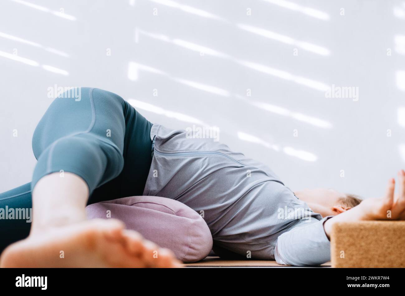 Woman doing yin yoga passive supine twists with bolster and cork block ...