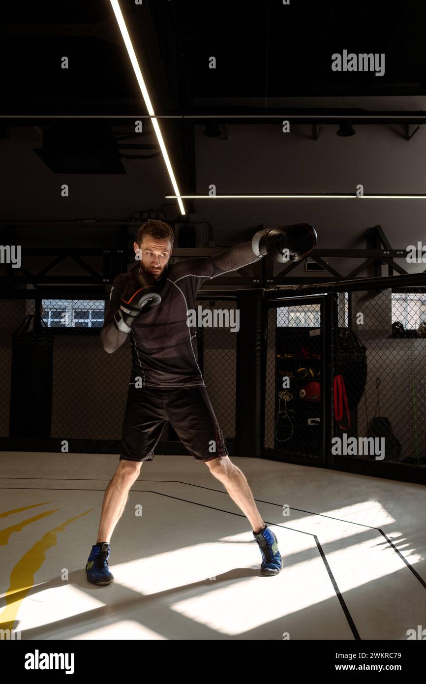 Concentrated boxer engaging in shadow boxing in empty dimly gym Stock ...