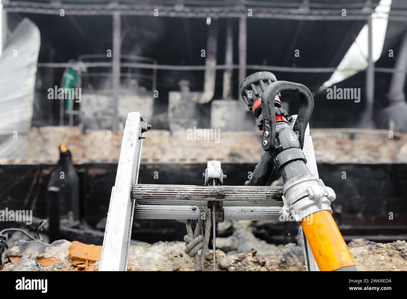 A fire hose lies on a ladder against the background of a burnt building ...