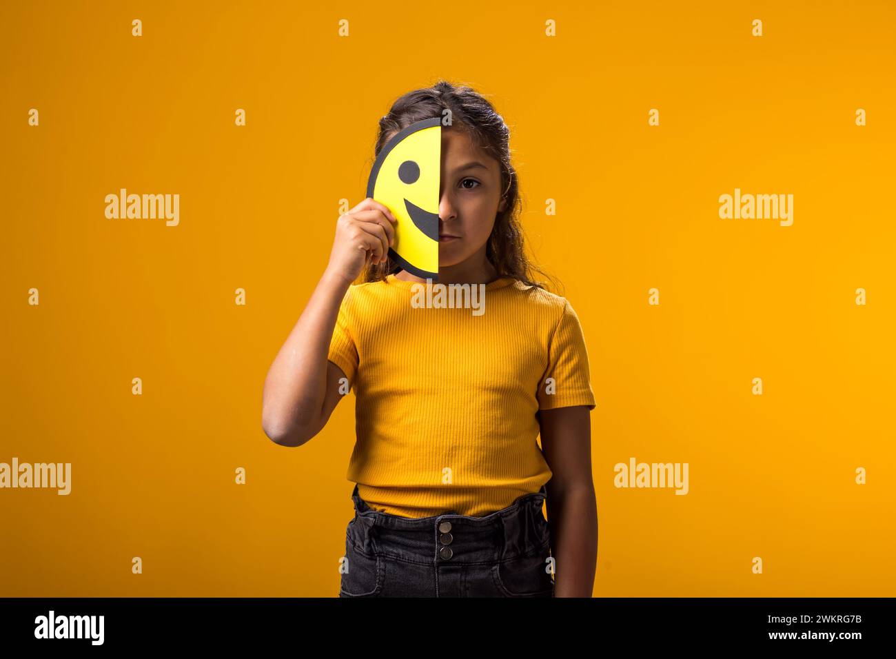 Portrait of sad kid girl holding happy half face emoticon. Mental ...