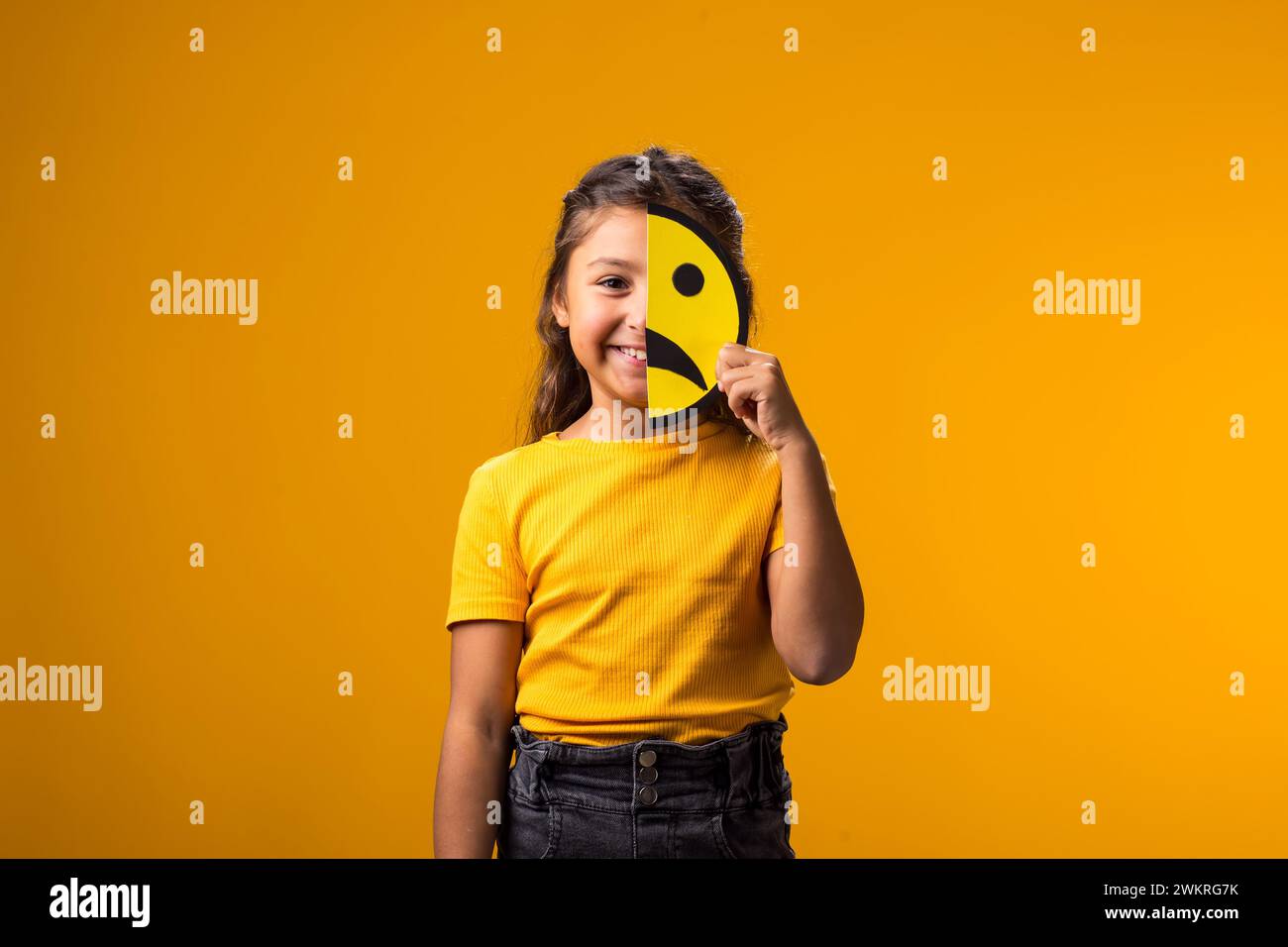 Portrait of smiling kid girl holding sad half face emoticon. Mental ...