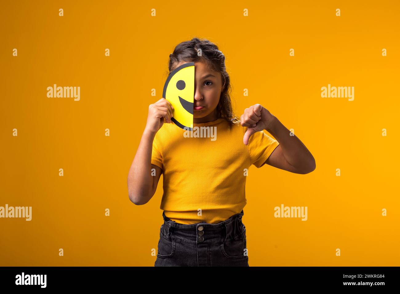 Portrait of sad kid girl holding happy half face emoticon. Mental ...