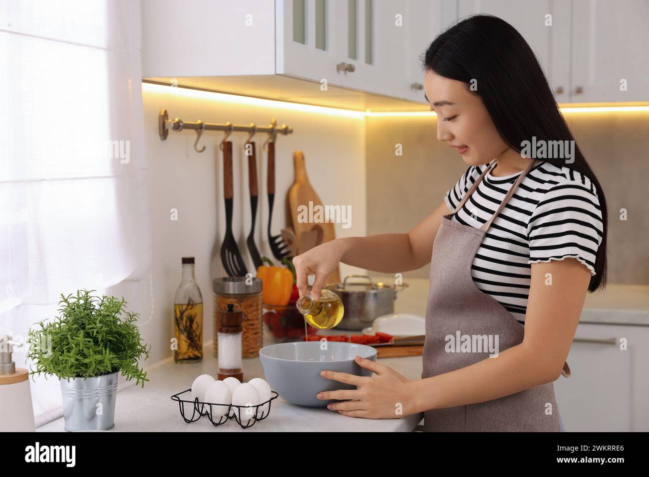 Cooking process. Beautiful woman pouring oil from bottle into bowl in ...