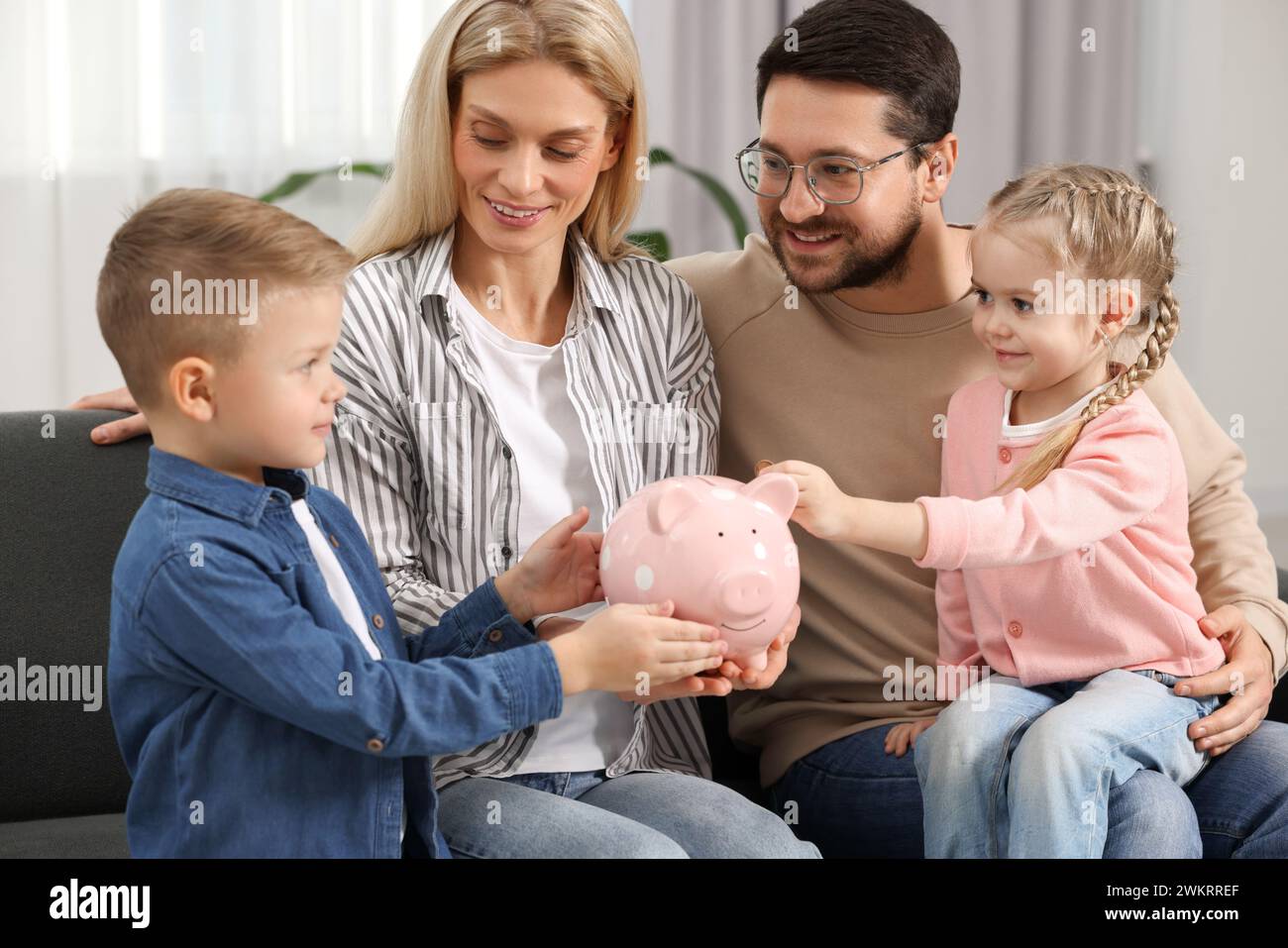Family budget. Little girl putting coin into piggy bank while her ...