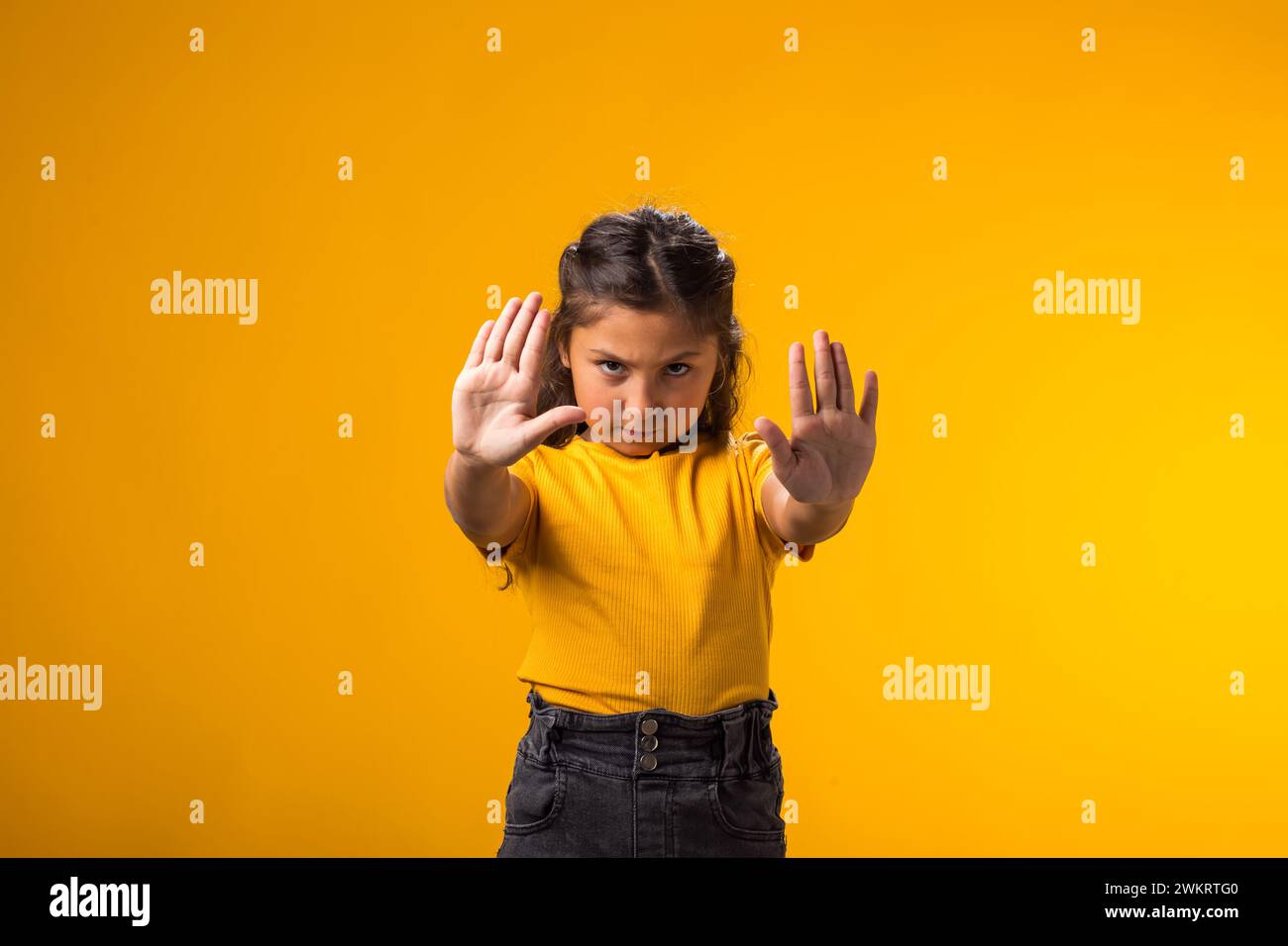 Portrait of child girl showing stop gesture on yellow background ...
