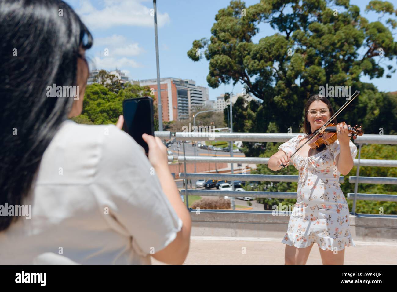 Unrecognizable woman is filming with her phone busker female violinist ...