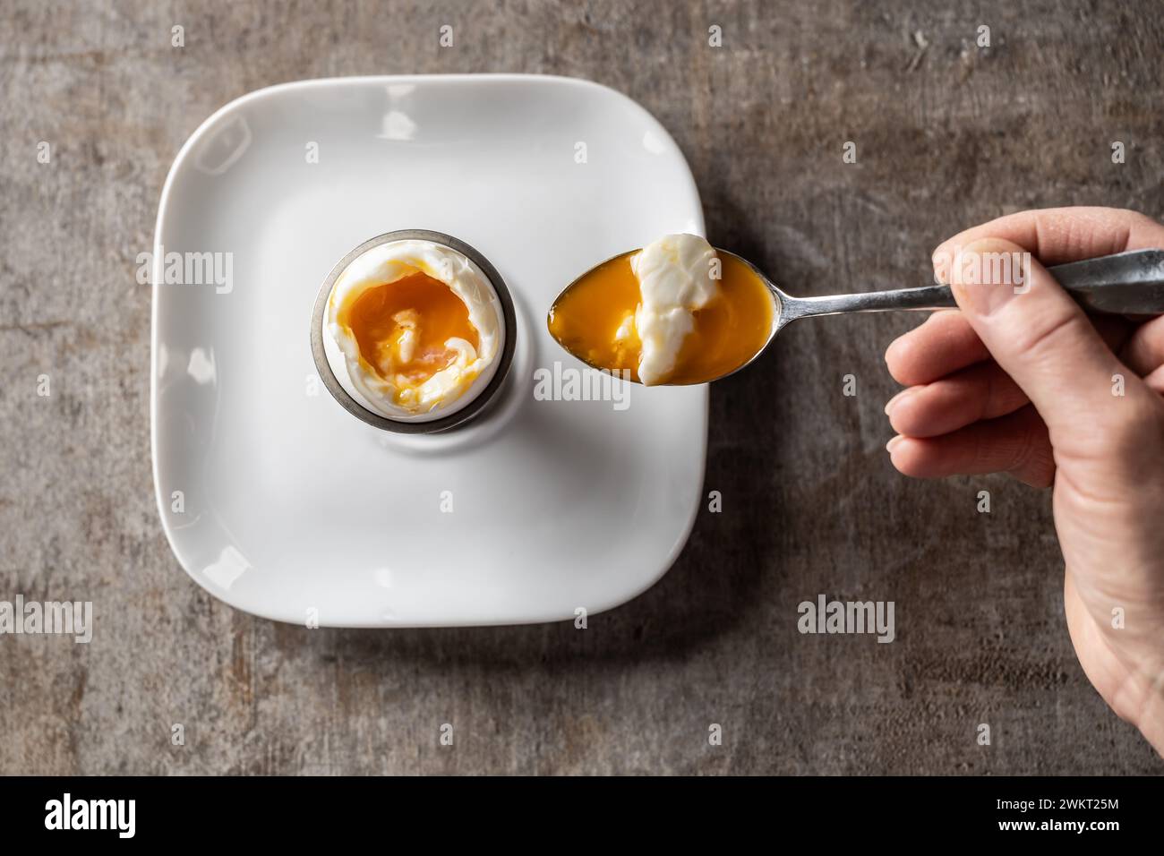 A woman's hand with a spoon scoops a soft-boiled egg from the shell ...