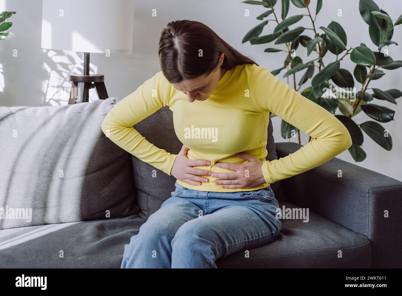 Sad young caucasian woman with stomach ache sitting on sofa at home ...