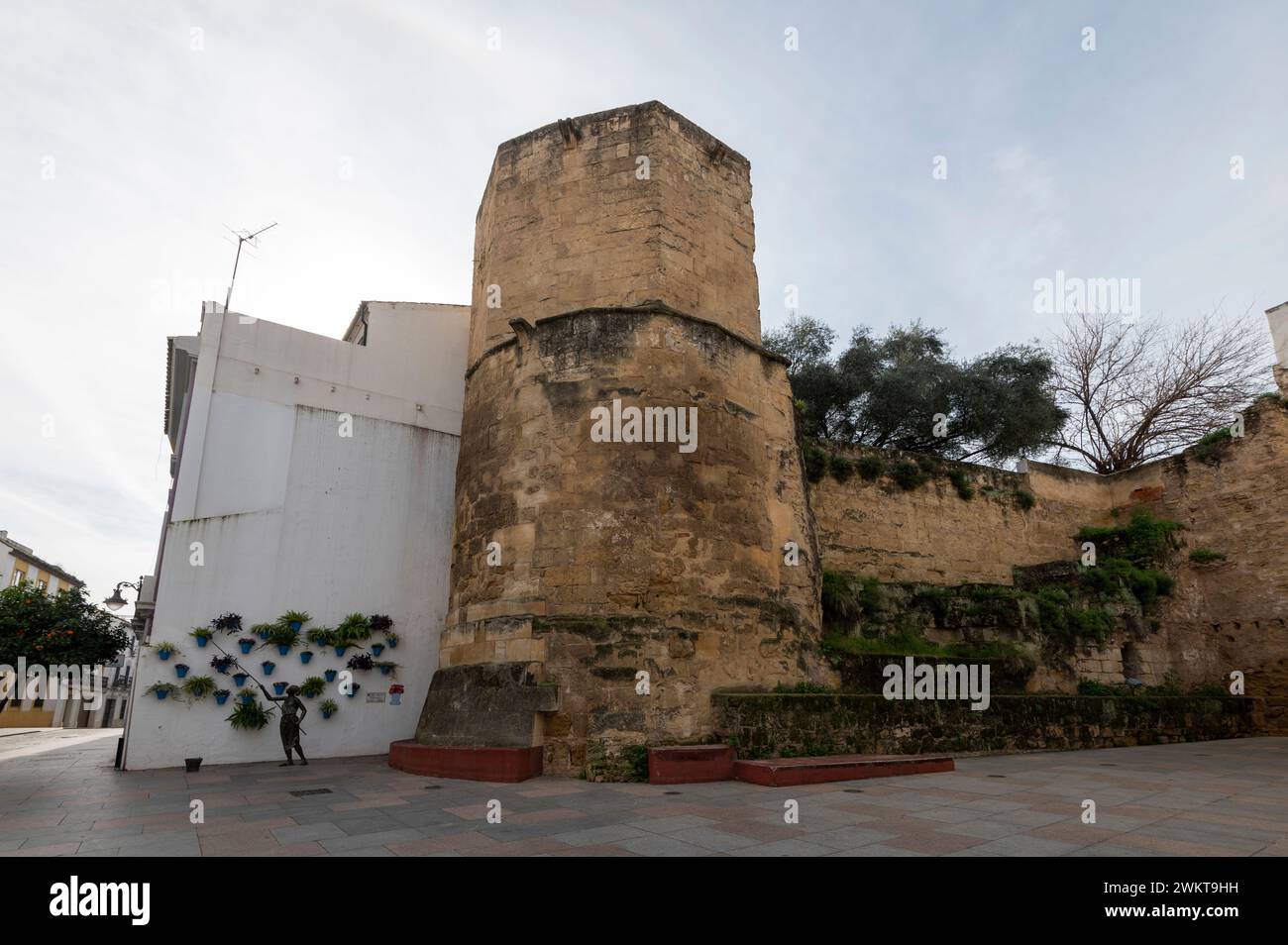 At the foot of a medieval tower is a sculpture of a woman watering her ...
