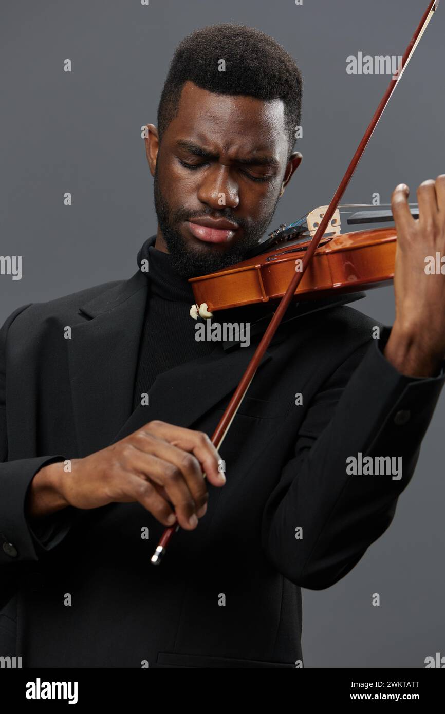 African American man in black suit playing violin on gray background in ...