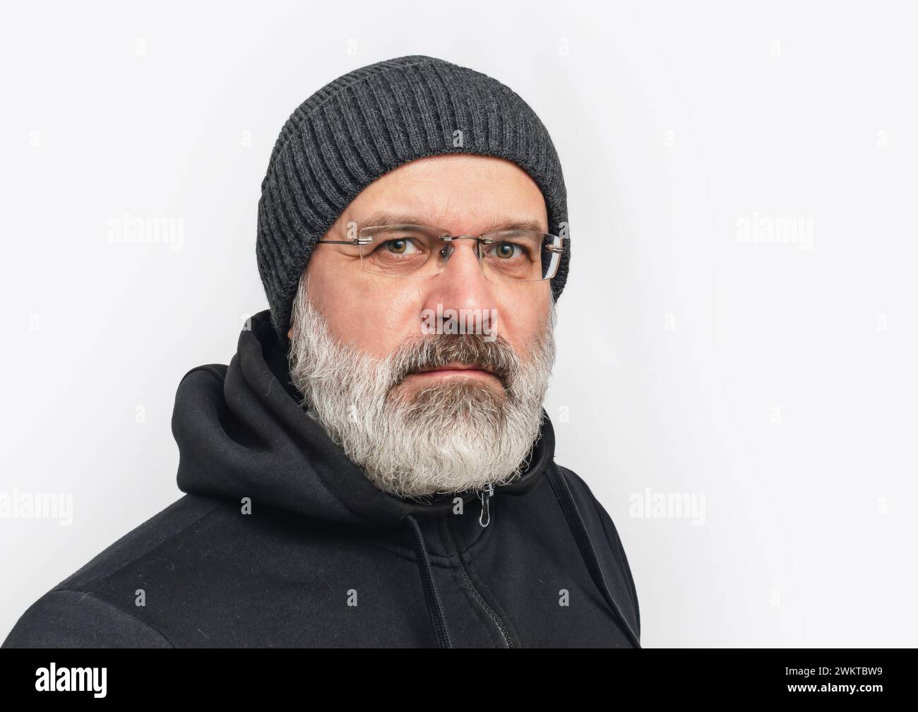 Serious man with gray beard and mustache in winter hat. Looks into camera. White background ...
