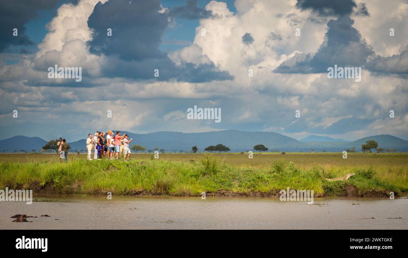 A group of tourists taking photos on smartphones crowd together to get ...