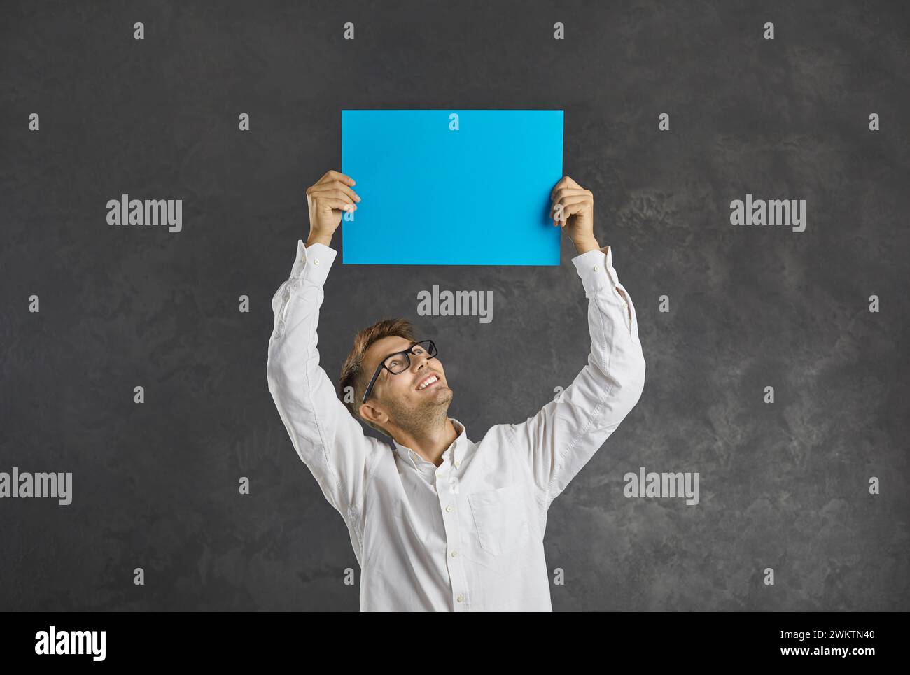 Happy smiling Caucasian man looks at a blank blue sheet of paper he is ...
