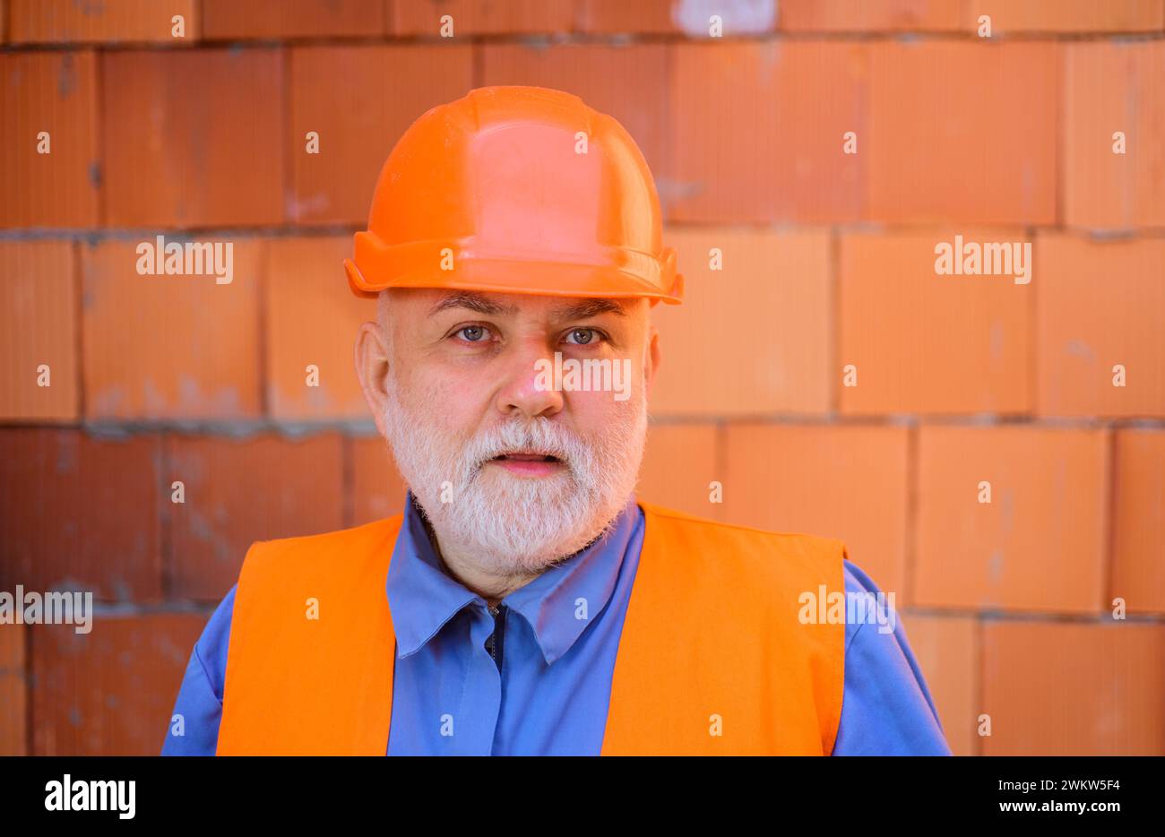 Portrait of serious construction worker in safety vest and helmet. Bearded architect builder in ...
