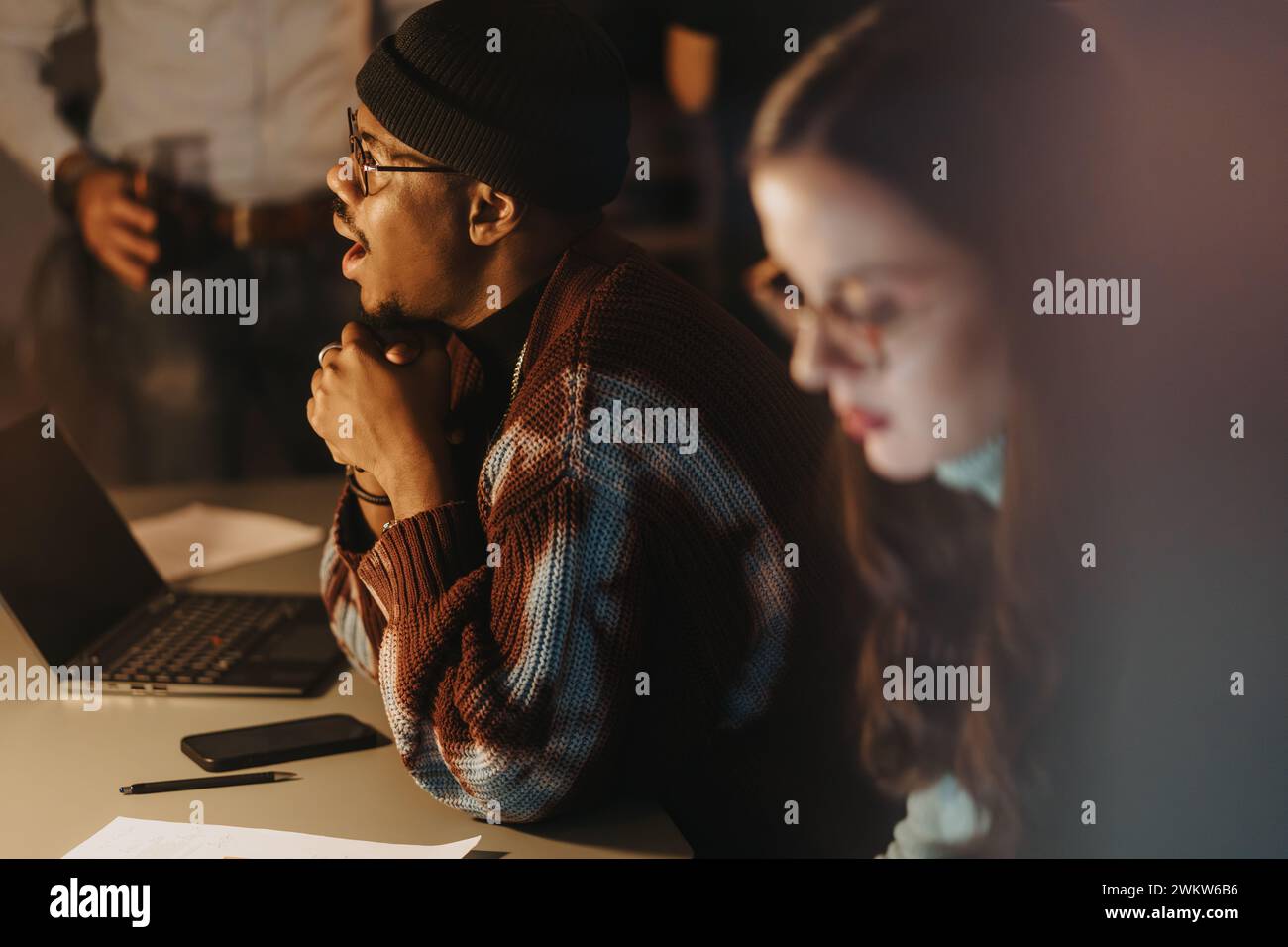 Two colleagues working intently in a dimly lit office space, expressing ...