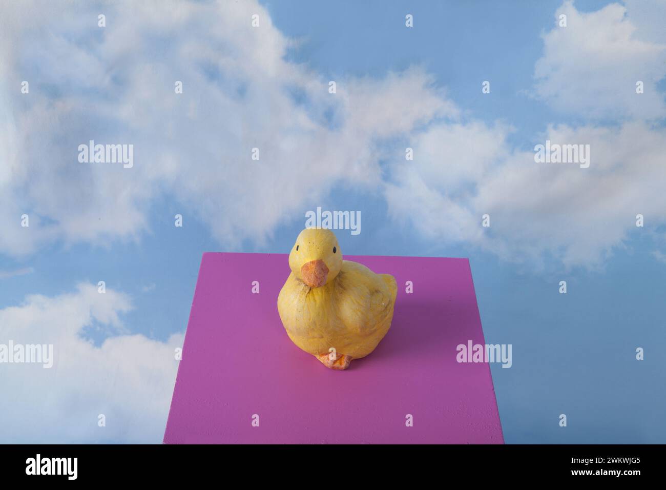a plaster duck on a pink cube in front of a blue sky with clouds ...