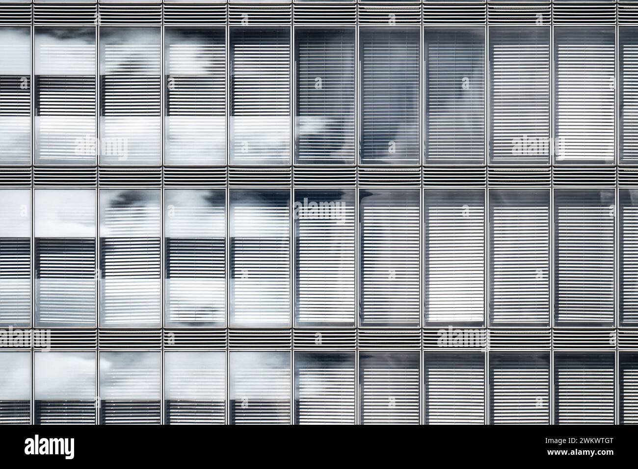 Light and clouds are reflected in the glass windows with blinds of a ...