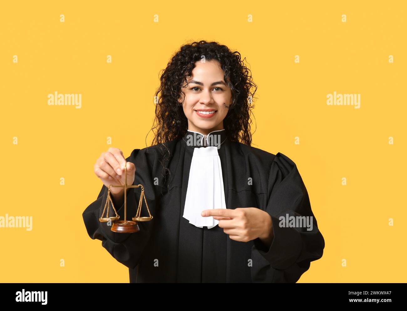 Beautiful young happy African-American female judge pointing at scales ...