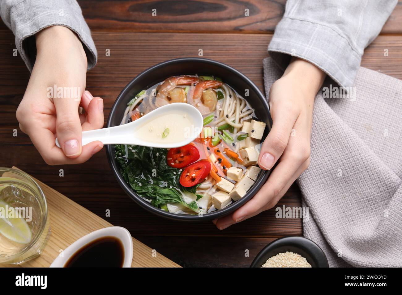 Woman eating delicious ramen with spoon at wooden table, top view ...
