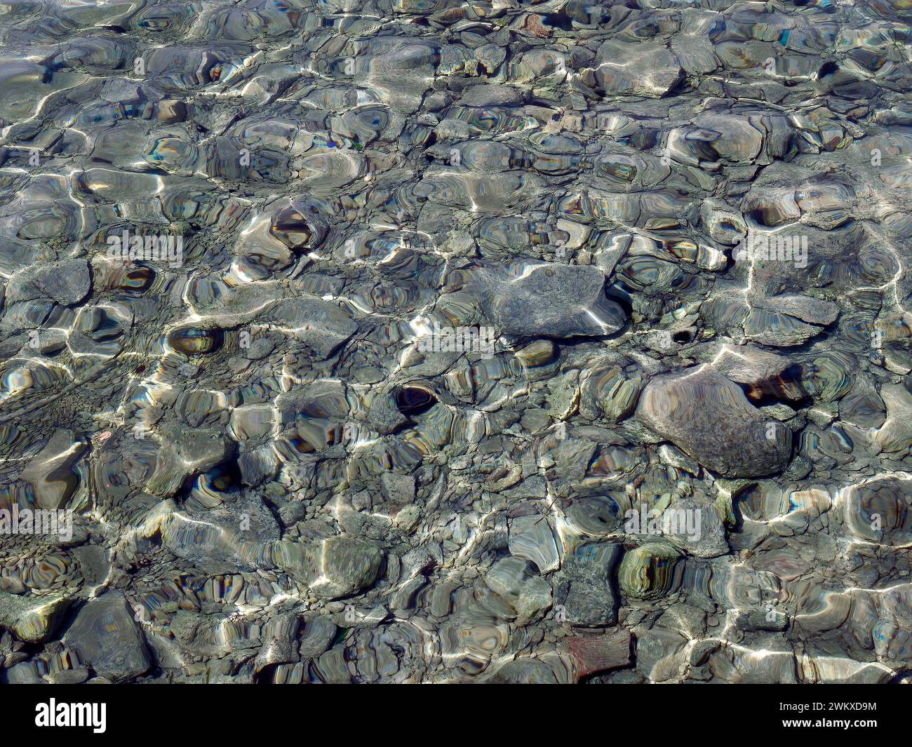 Pebble rocks in the crystal clear water with shadow line, see through ...