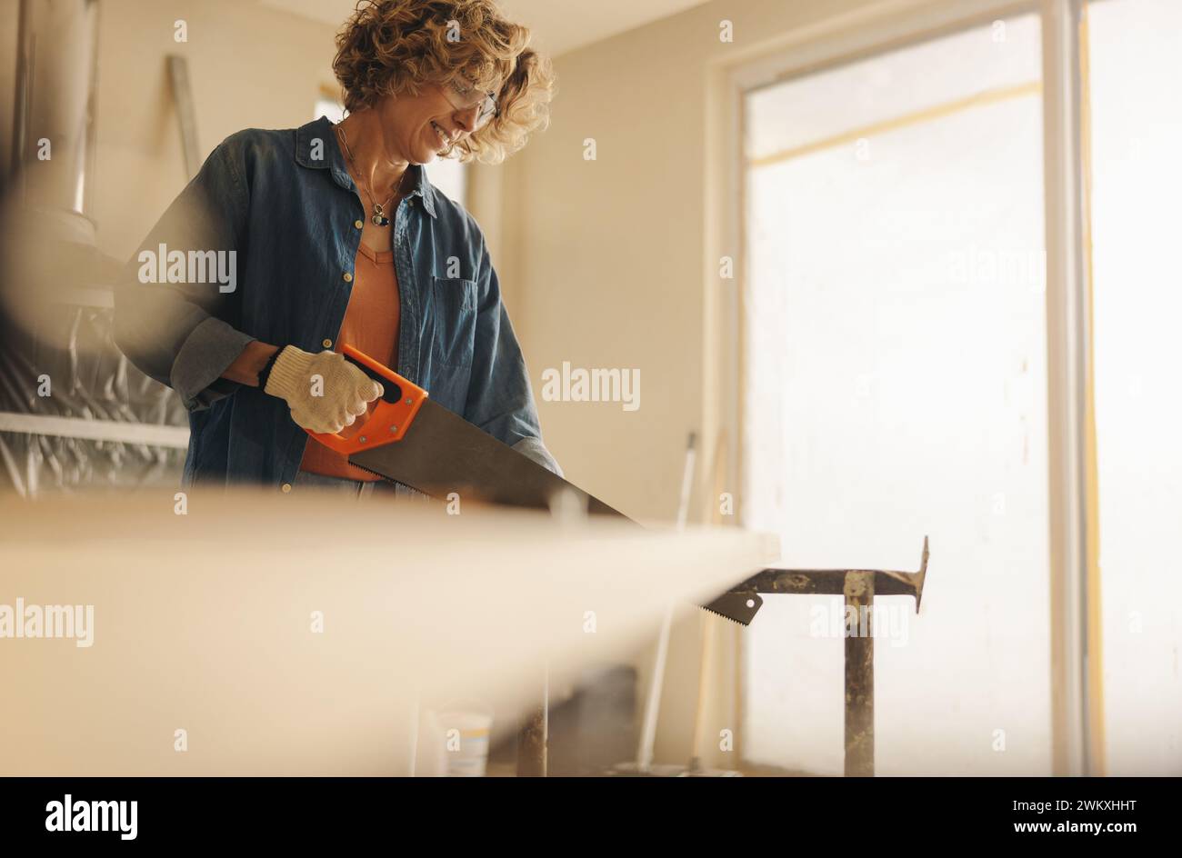 Woman renovates her kitchen, using a saw to cut baseboards for trim ...