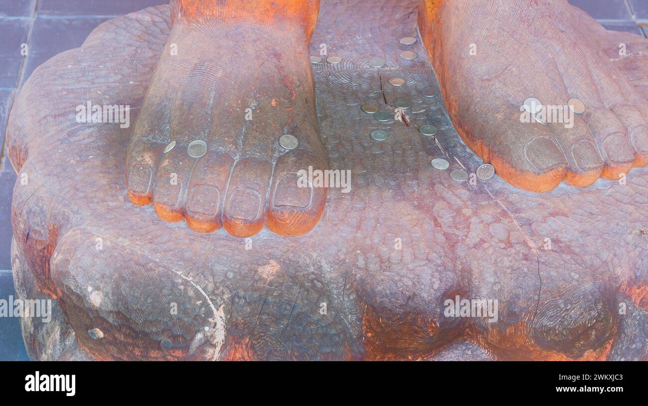 Coins laying on the feet of a wooden statue on top of plinth in South ...