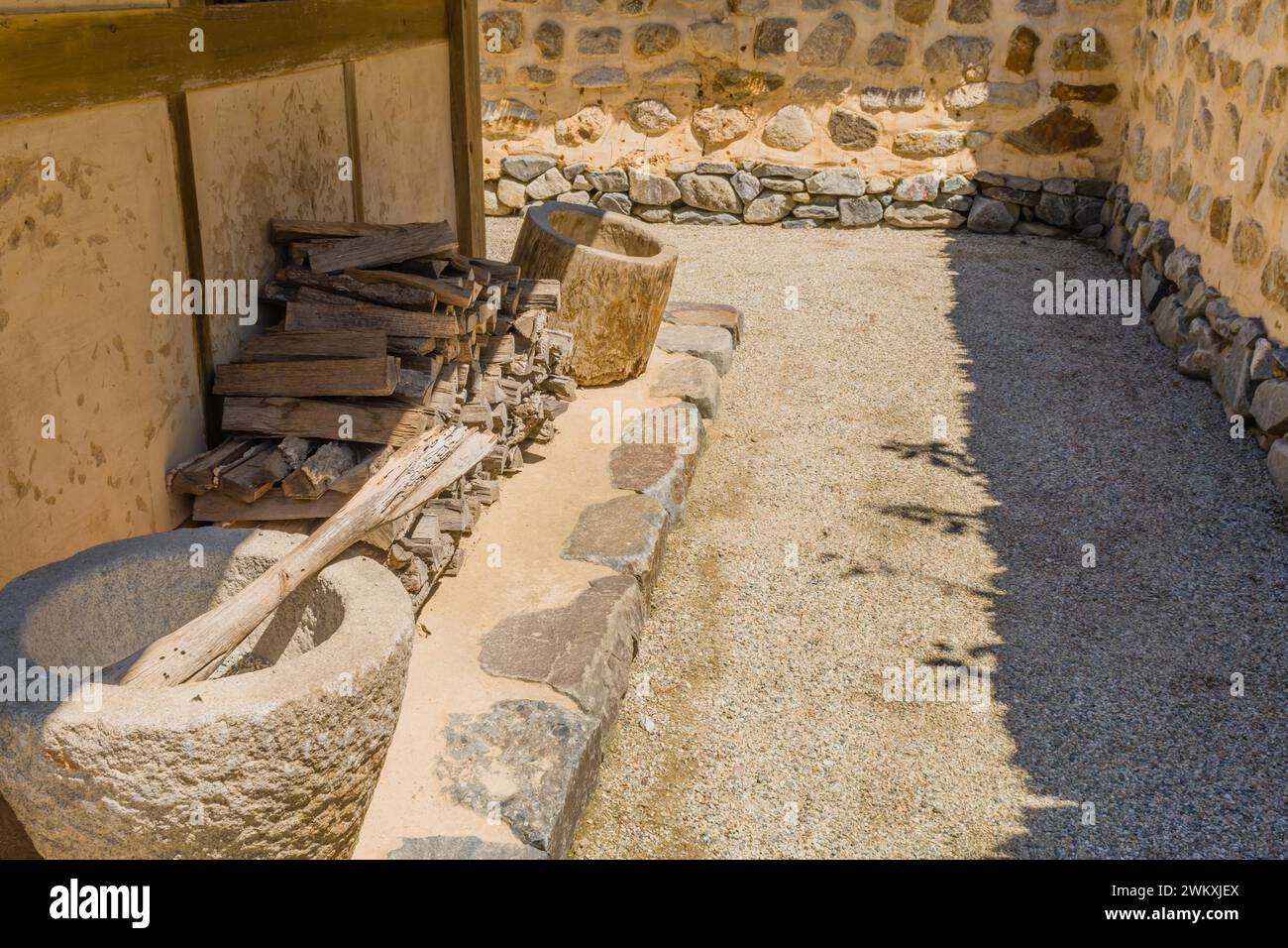 Chopped word and stone grinding pot next to wall of traditional house ...