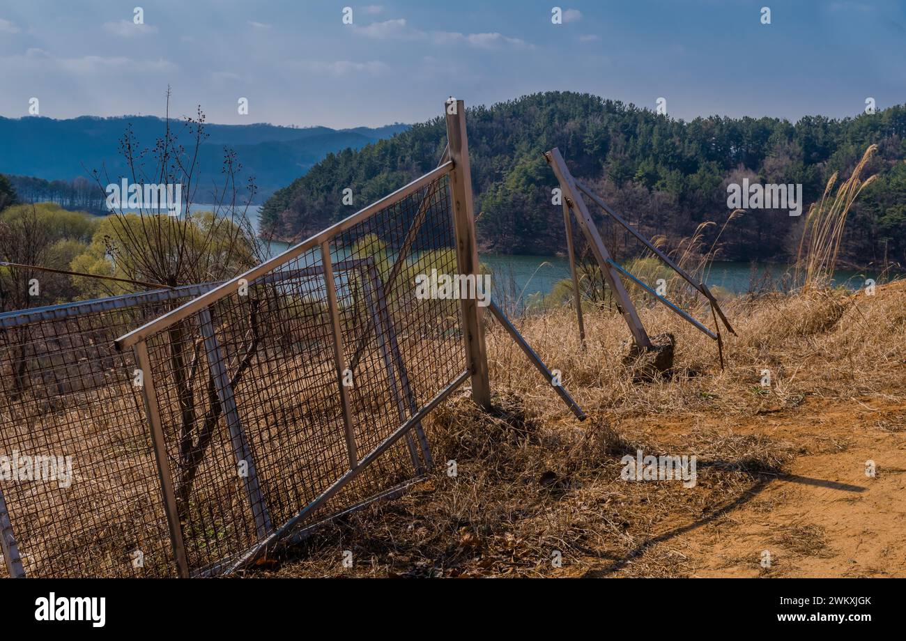 Broken metal gate and post sitting in field with lake and mountains in ...