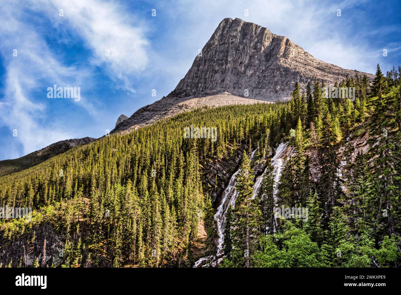 Waterfall cascading into rocky river at base of towering mountain Stock ...