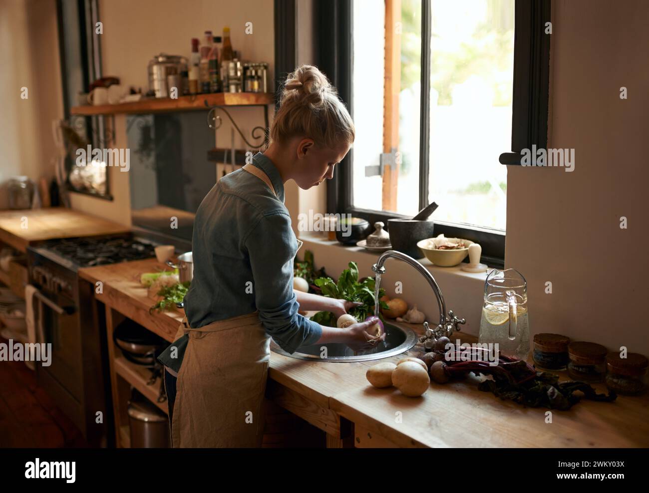 Woman, chef and washing food for hygiene in the kitchen sink at home ...