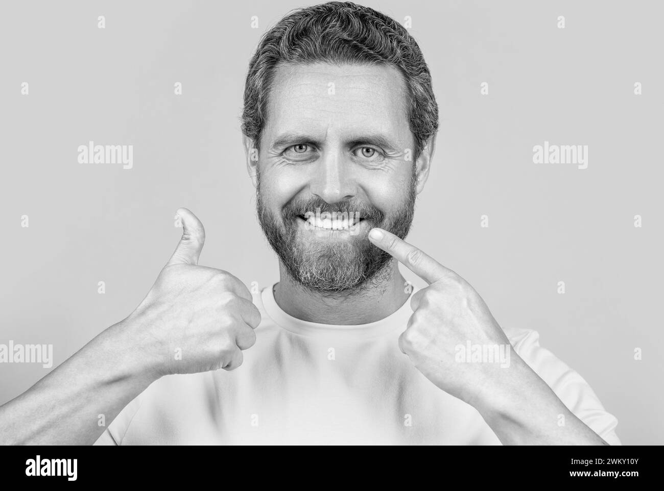 smiling man pointing at teeth smile in studio, thumb up. photo of man ...