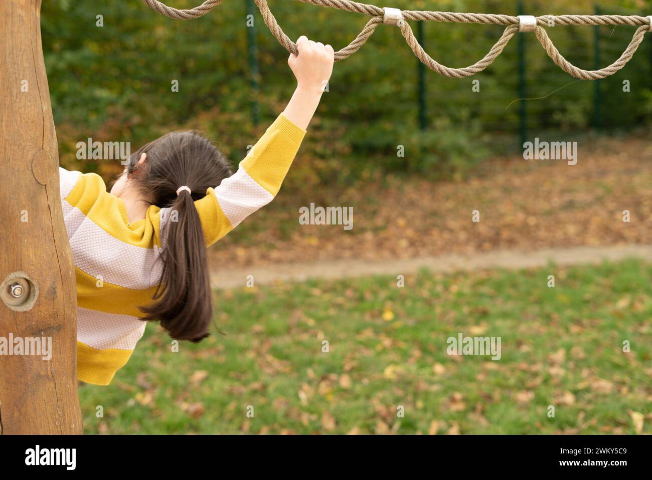 Little girl climbing on a rope in a park. Back view Stock Photo - Alamy