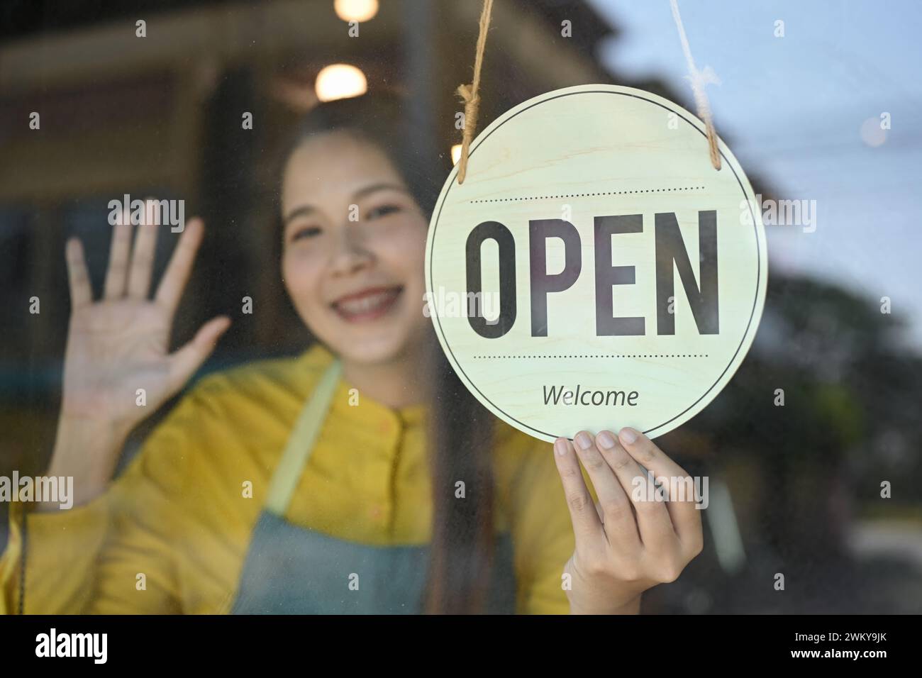 Smiling female small business owner wearing apron turning open sign on ...