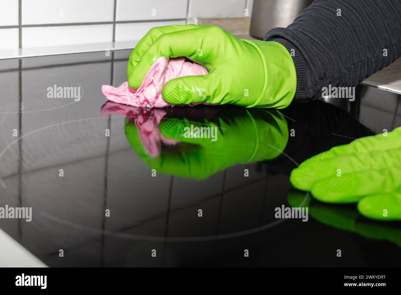 A person in rubber gloves cleaning the induction hob and using cloth ...