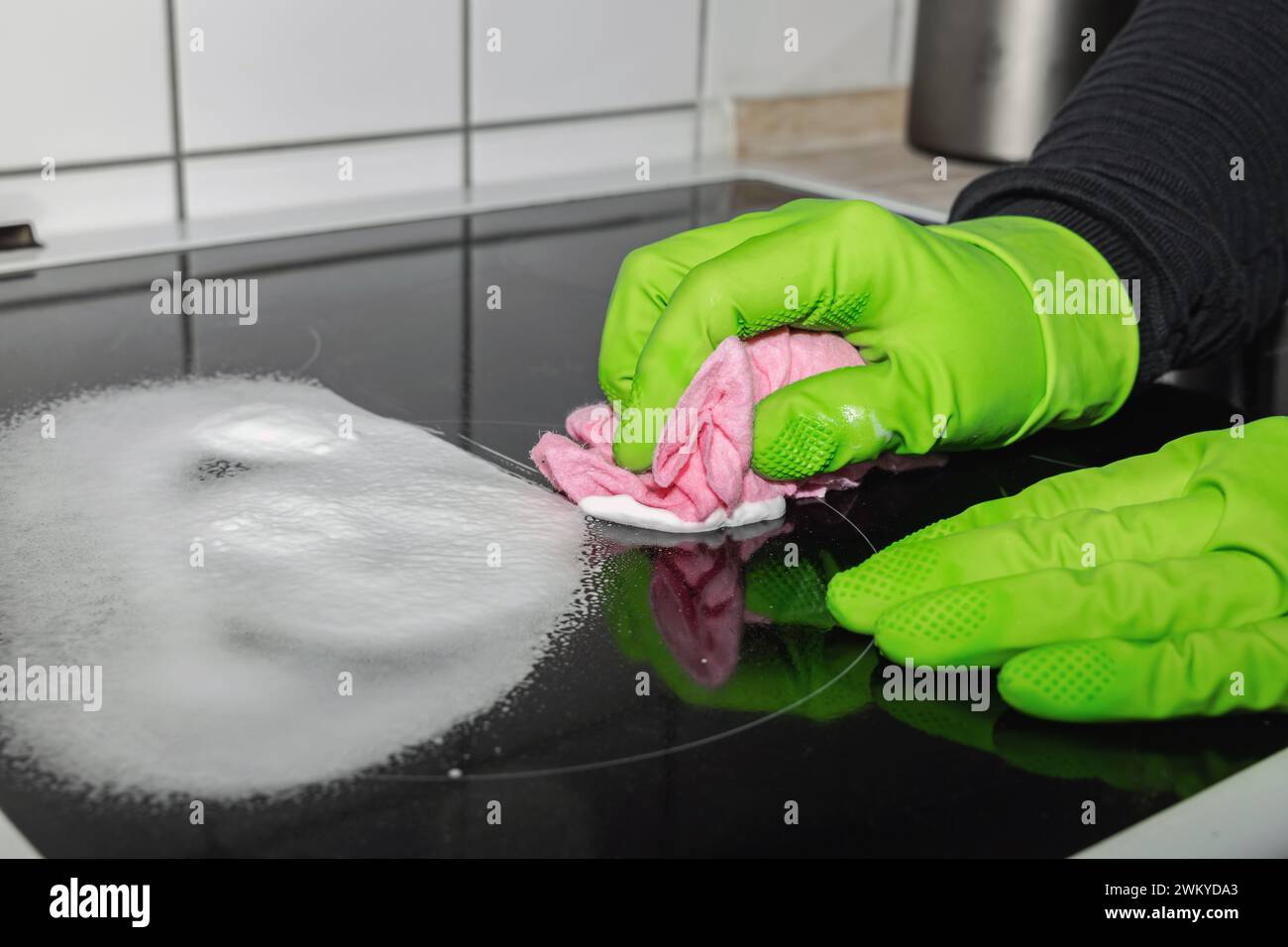 A person in rubber gloves cleaning the induction hob and using cloth ...