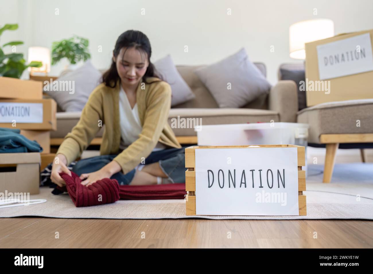 Asian young woman packing clothes at home, putting on stuff into donate ...