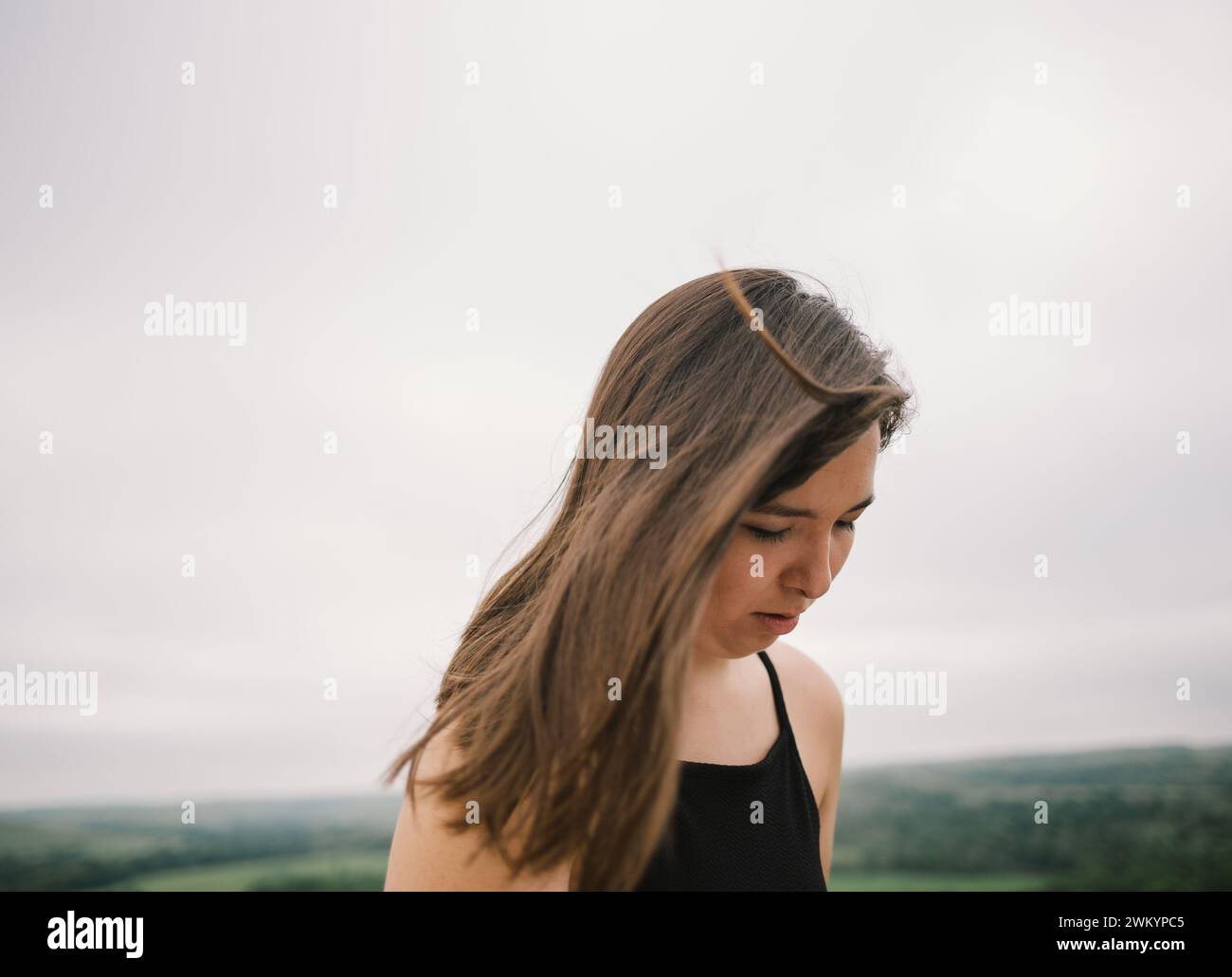 Young half-Asian woman with wind blown hair looks down while outdoors ...