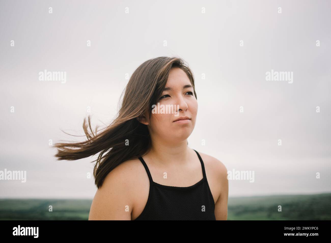 Young half-Asian woman looks off into distance while wind blows her ...