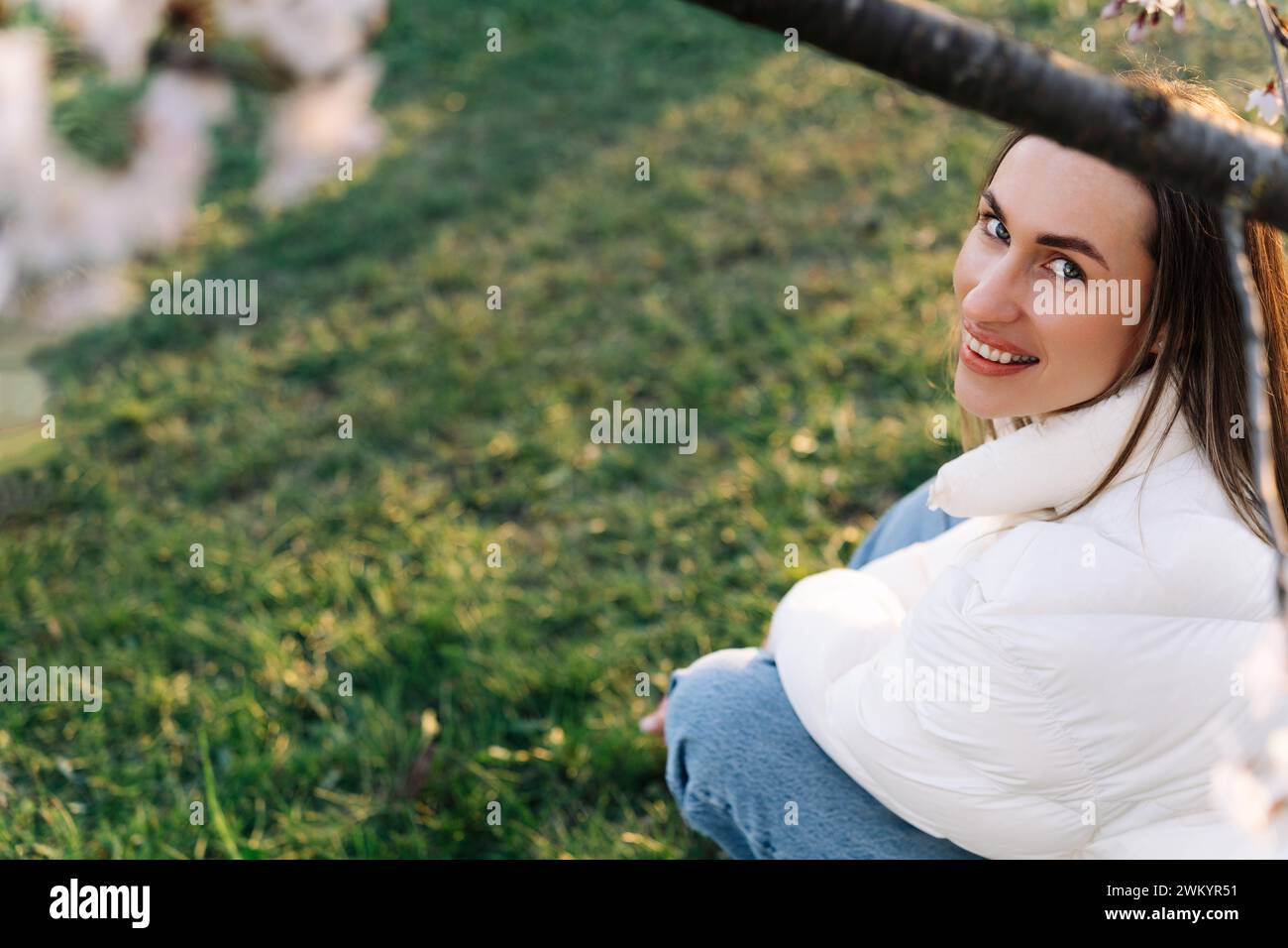 Woman enjoying spring sitting on grass in city park under cherry ...
